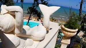 Uma área na piscina com uma grande escultura branca, um vaso de planta e vista para a praia.