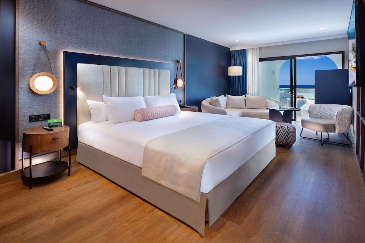 Quarto de hotel moderno com uma cama grande, um sofá, uma mesinha e vista para o oceano.