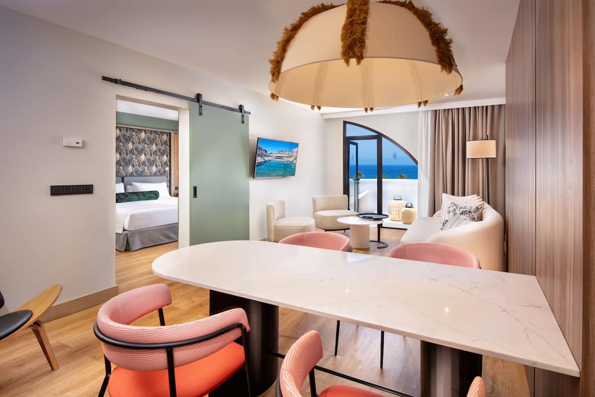 Quarto de hotel moderno com área de refeições, sofá e vista para o mar.