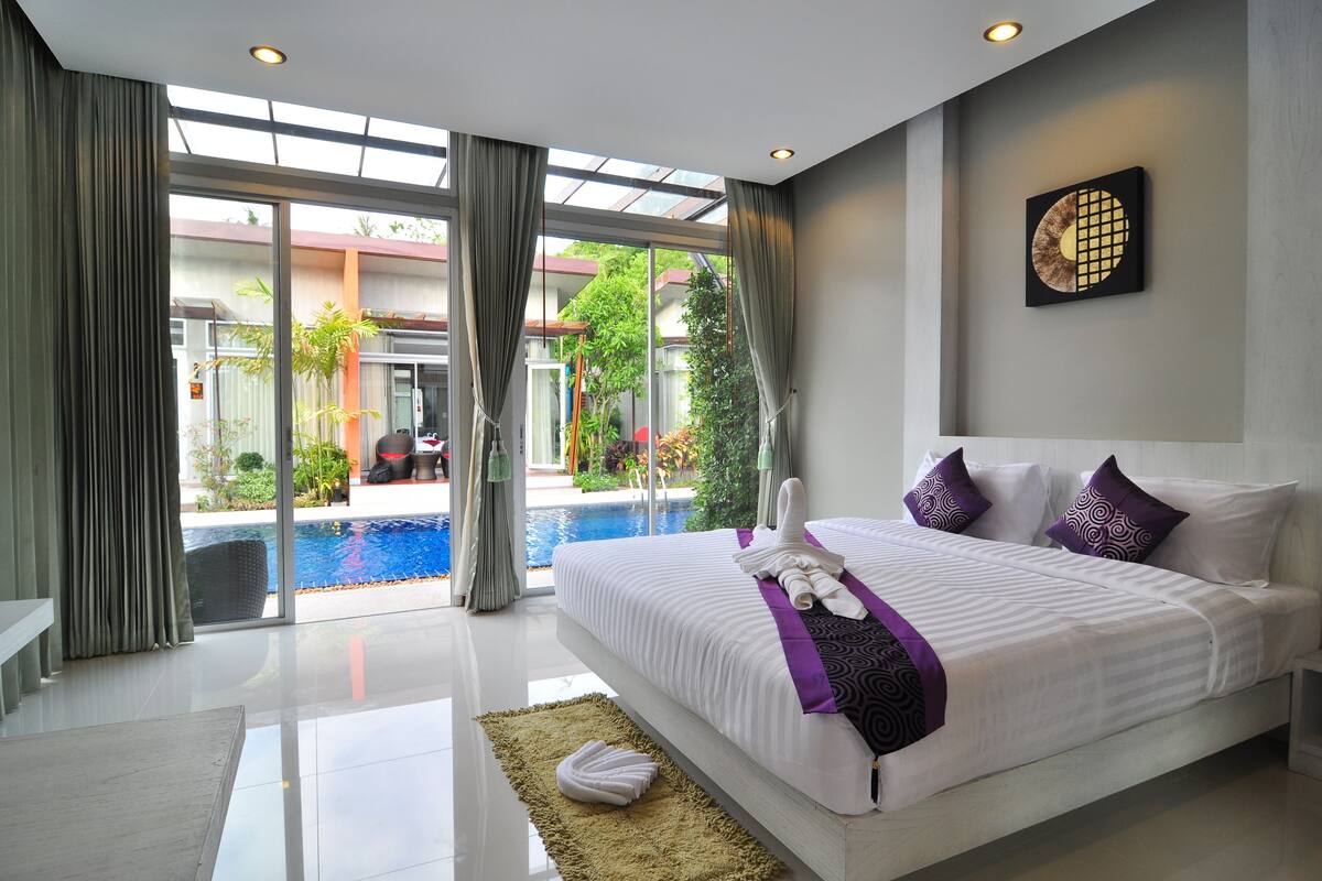 Quarto de hotel moderno com uma cama grande, vista para uma piscina ao ar livre e porta de vidro que dá para a área da piscina.