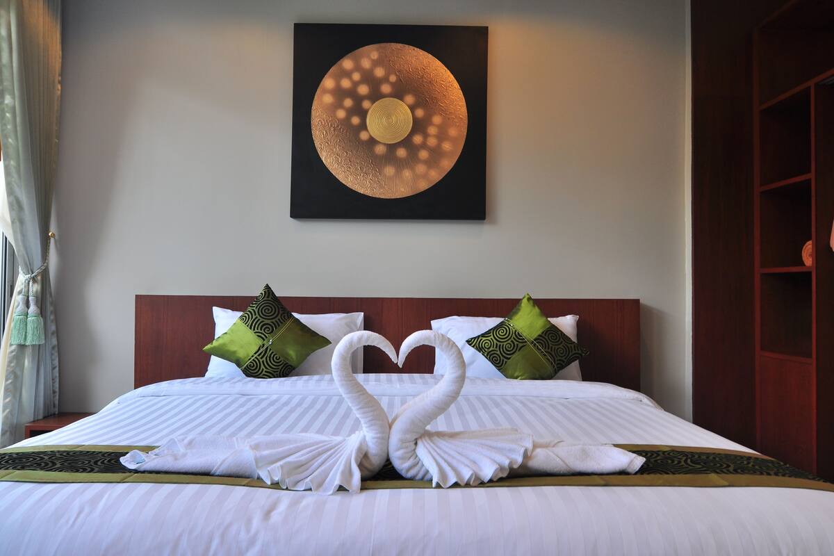 Quarto de hotel com cama bem arrumada, duas almofadas, uma obra de arte na parede e cabeceira de madeira.