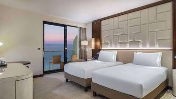 Quarto de hotel com duas camas, uma escrivaninha, um minibar e vista para o mar.