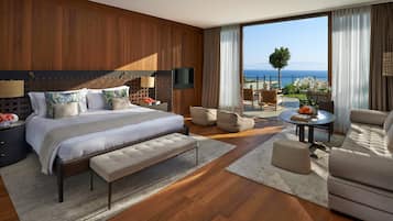 Quarto de hotel moderno com uma cama grande, área de estar com uma mesa e varanda com vista para o mar.