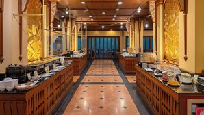 Uma área de buffet com um balcão longo, diversas estações de comida e painéis decorativos na parede.