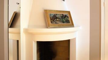 Uma lareira com um quadro emoldurado acima, um espelho na parede à esquerda e uma porta à direita.