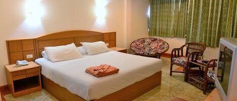 Quarto de hotel com cama de madeira, mesa de cabeceira, uma cadeira e uma televisão.
