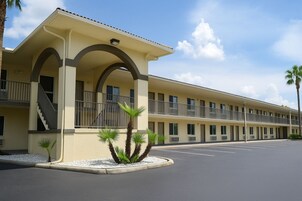 Um motel com vários andares e um pátio central, apresentando uma galeria coberta, varandas e um estacionamento.