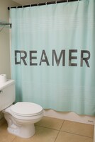 Um banheiro com vaso sanitário, cortina de chuveiro com a palavra 'DREAMER' estampada e um porta-toalhas acima do vaso.