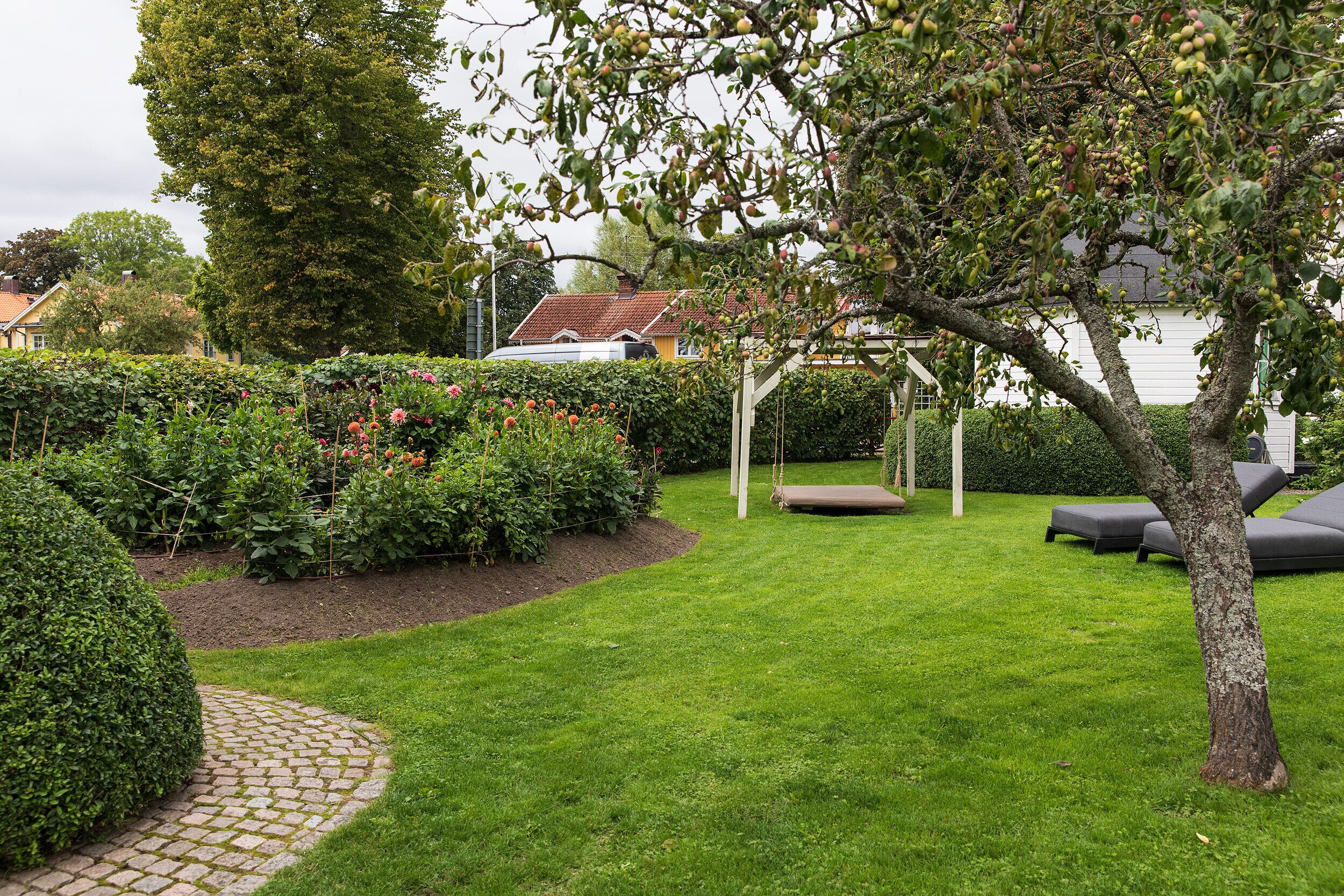 Um jardim bem cuidado com um caminho pavimentado, sebes podadas e uma área de estar com pérgola.