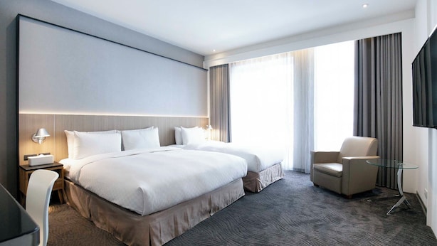 Quarto de hotel moderno com uma cama grande, uma escrivaninha, uma cadeira e uma televisão.