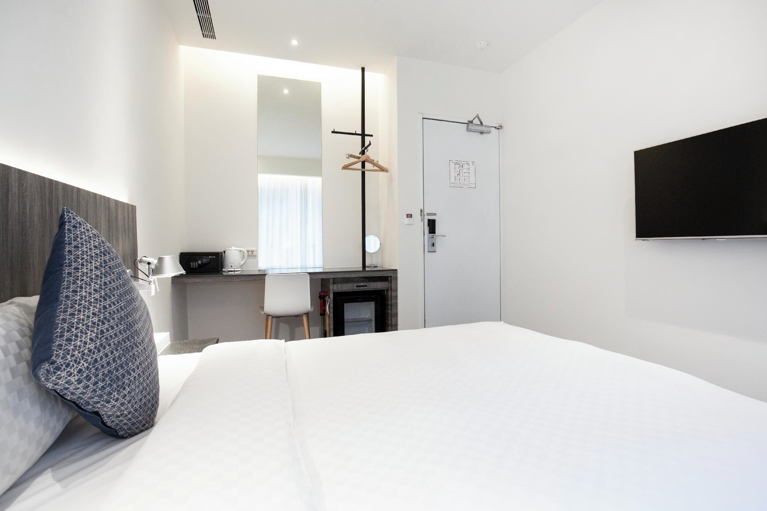 Quarto de hotel com cama, escrivaninha, cadeira, televisão e guarda-roupa.