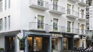 Hotel com vários andares, varandas, entrada no andar térreo e uma fileira de scooters estacionadas.