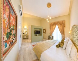 Quarto de hotel com cama, televisão, escrivaninha e banheiro visível por uma porta aberta.