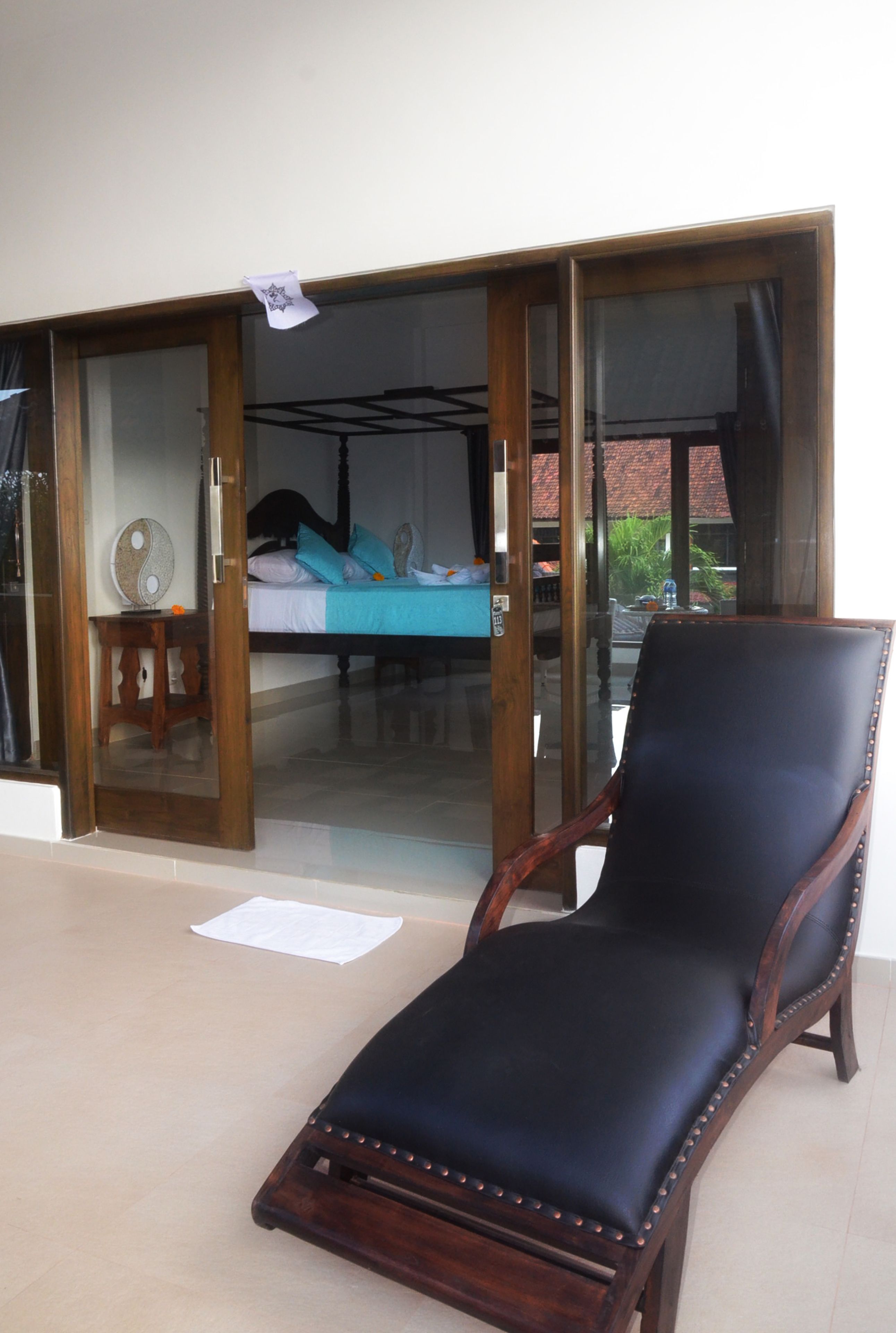 Quarto com cama, uma cadeira e porta de vidro deslizante para área externa.