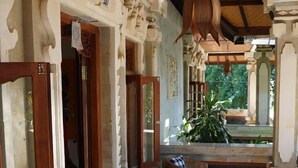 Uma área externa coberta com móveis de vime, luminária pendente e vista para o verde.