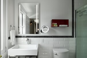 Uma casa de banho moderna com uma sanita, um lavatório branco, um espelho iluminado e uma prateleira vermelha com artigos de higiene pessoal.