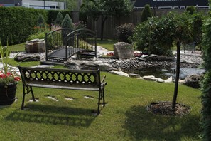 Um jardim com um banco, uma pequena ponte e um lago.