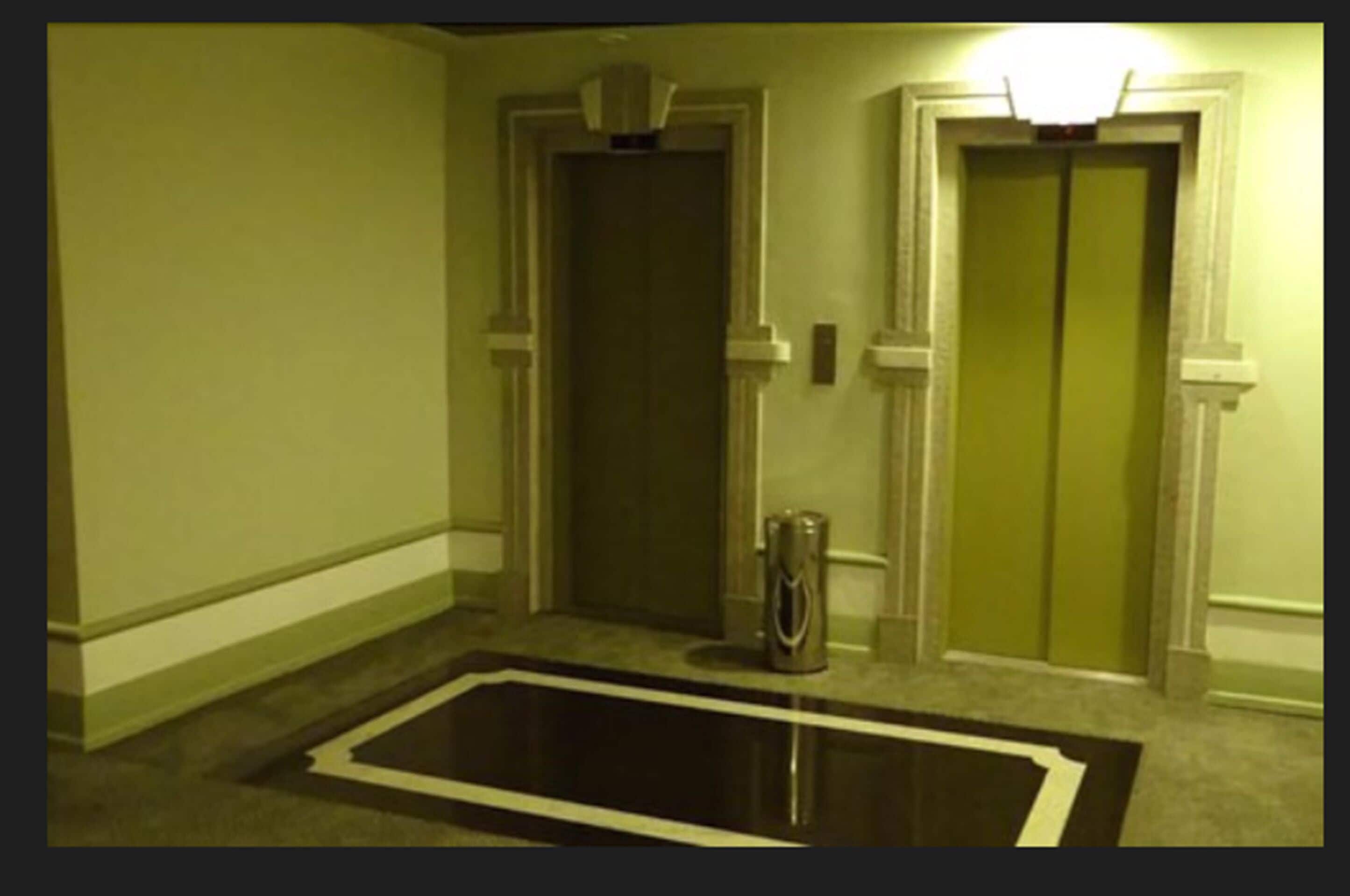 Um corredor com dois elevadores, uma máquina de café e piso coberto de carpete.