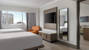 Quarto de hotel com duas camas, televisão, escrivaninha e uma grande janela com vista para a cidade.