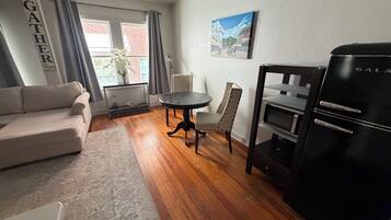 Uma sala de estar com sofá, mesa de jantar com cadeiras, geladeira preta e um quadro na parede.