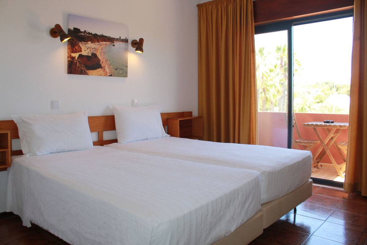 Uma cama de casal com roupa de cama branca, cabeceira de madeira e um quadro acima.