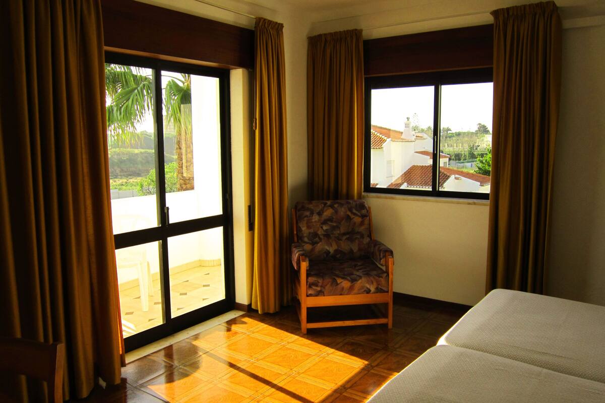 Quarto de hotel com uma janela grande, uma cadeira e uma cama.