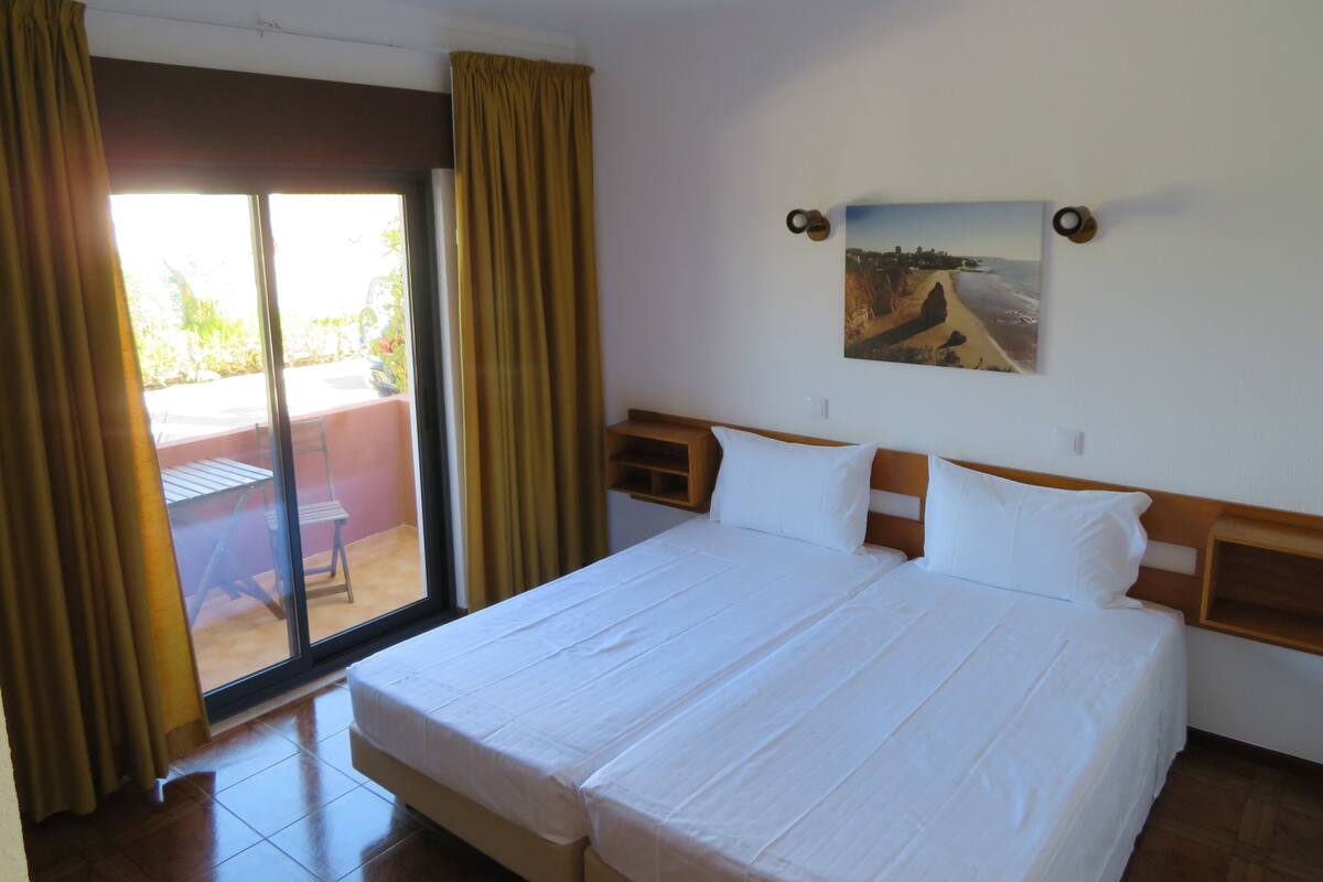 Quarto de hotel com uma cama grande, porta de vidro deslizante para uma varanda e um quadro na parede.