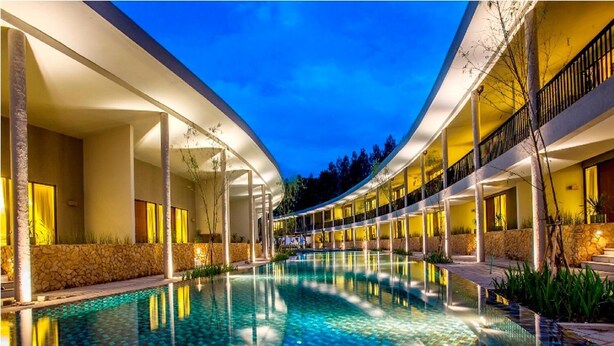 Área de piscina com estrutura de prédio curvilínea, paredes de pedra e piscina azul cristalina.