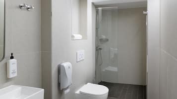 Uma casa de banho moderna com lavatório branco, sanita e área de duche.