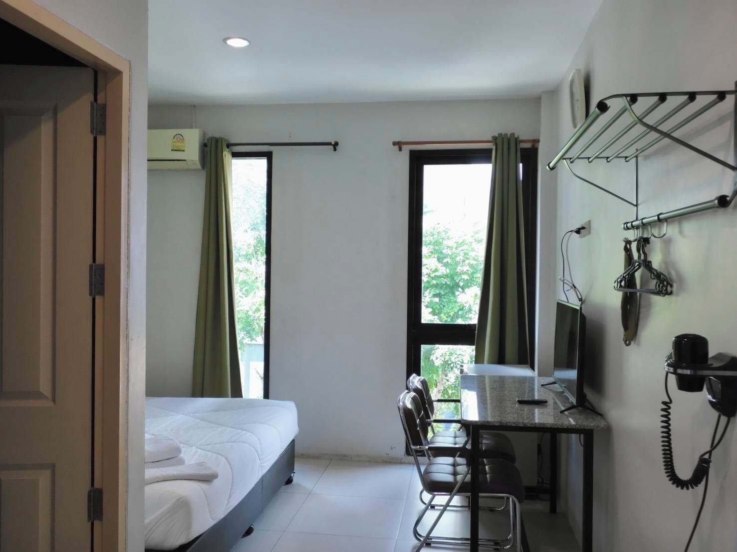 Quarto de hotel com cama, escrivaninha, cadeira, telefone e janela com cortinas.