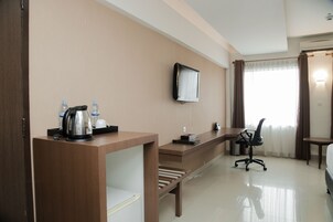 Quarto de hotel com uma secretária de madeira, televisão fixada na parede, cama, cadeira e janela com cortinas.