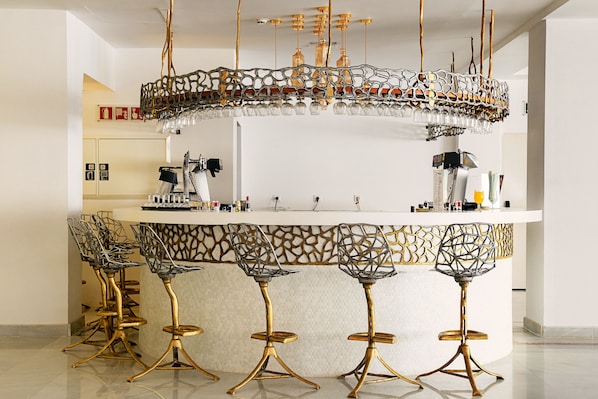 Uma área de bar com um lustre singular, banquetas e um balcão branco.