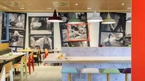 Um café moderno com cadeiras coloridas, uma área de bar central e fotografias a preto e branco nas paredes.