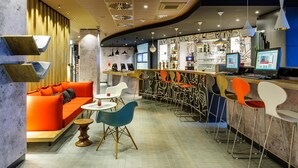 Uma área de bar moderna com um balcão curvo, vários bancos altos e um espaço de estar com um sofá e cadeiras.