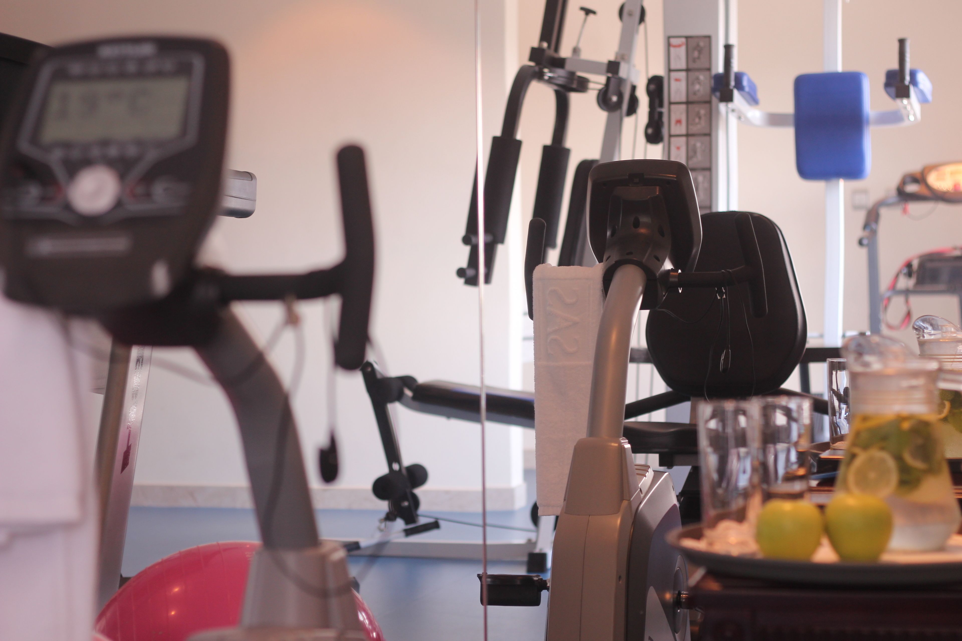 Academia com equipamentos de ginástica, esteira e garrafa de água com limões em uma mesa.