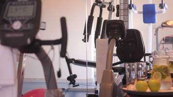 Academia com equipamentos de ginástica, esteira e garrafa de água com limões em uma mesa.