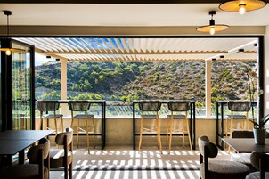 Um restaurante com área externa, grandes janelas e vista para uma paisagem montanhosa.