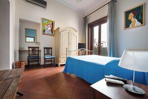 Quarto de hotel com cama, escrivaninha, cadeira, luminária e janela com cortinas.