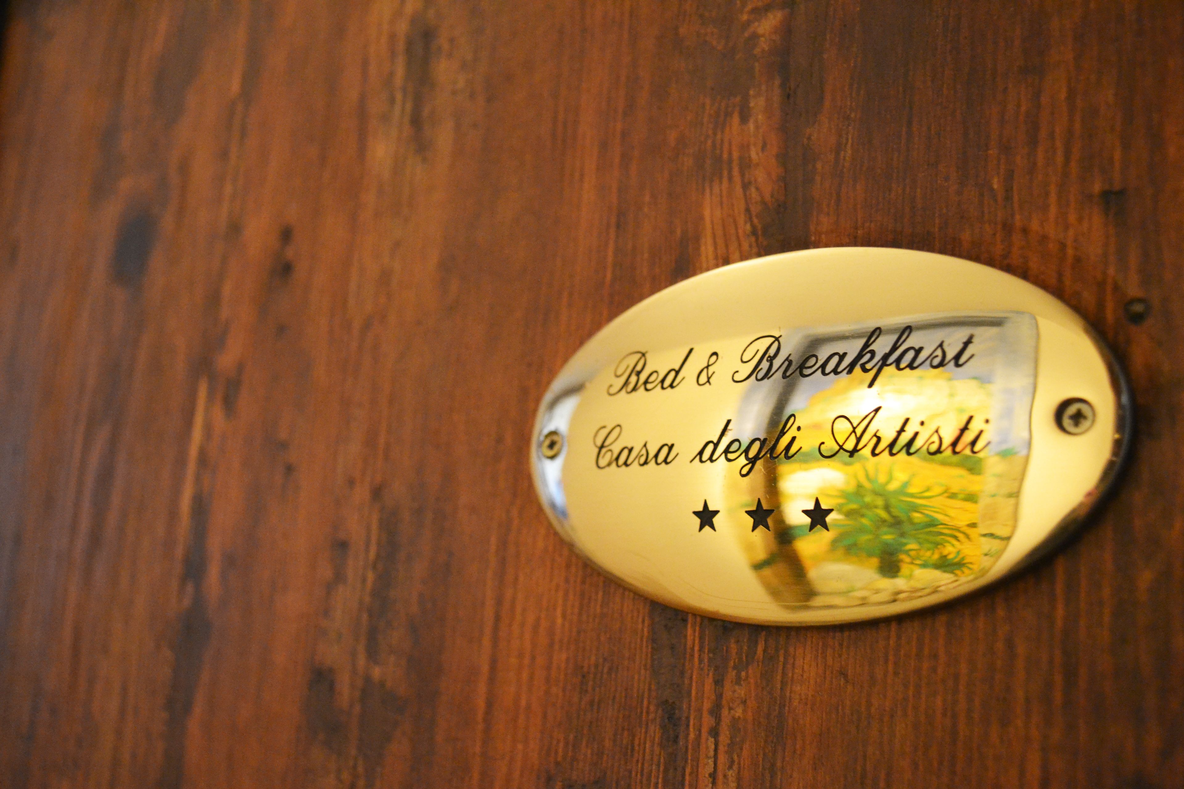 Uma placa de latão com a inscrição 'Bed & Breakfast Casa degli Artisti' sobre uma superfície de madeira.
