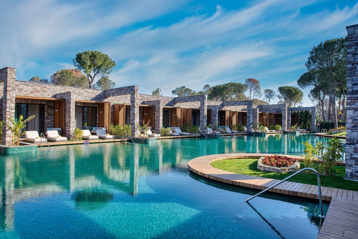 Área de piscina com edifícios de pedra, espreguiçadeiras e uma piscina azul cristalina.