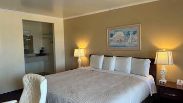 Quarto de hotel com cama, duas luminárias de cabeceira, um quadro, mesa de cabeceira e uma cadeira.