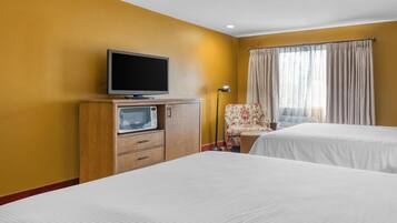 Quarto de hotel com duas camas, uma televisão sobre um armário de madeira, micro-ondas e uma cadeira com estofamento floral.