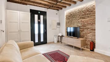 Uma sala de estar moderna com um sofá, uma TV sobre um móvel de madeira, uma parede de tijolos e uma porta com um aviso.