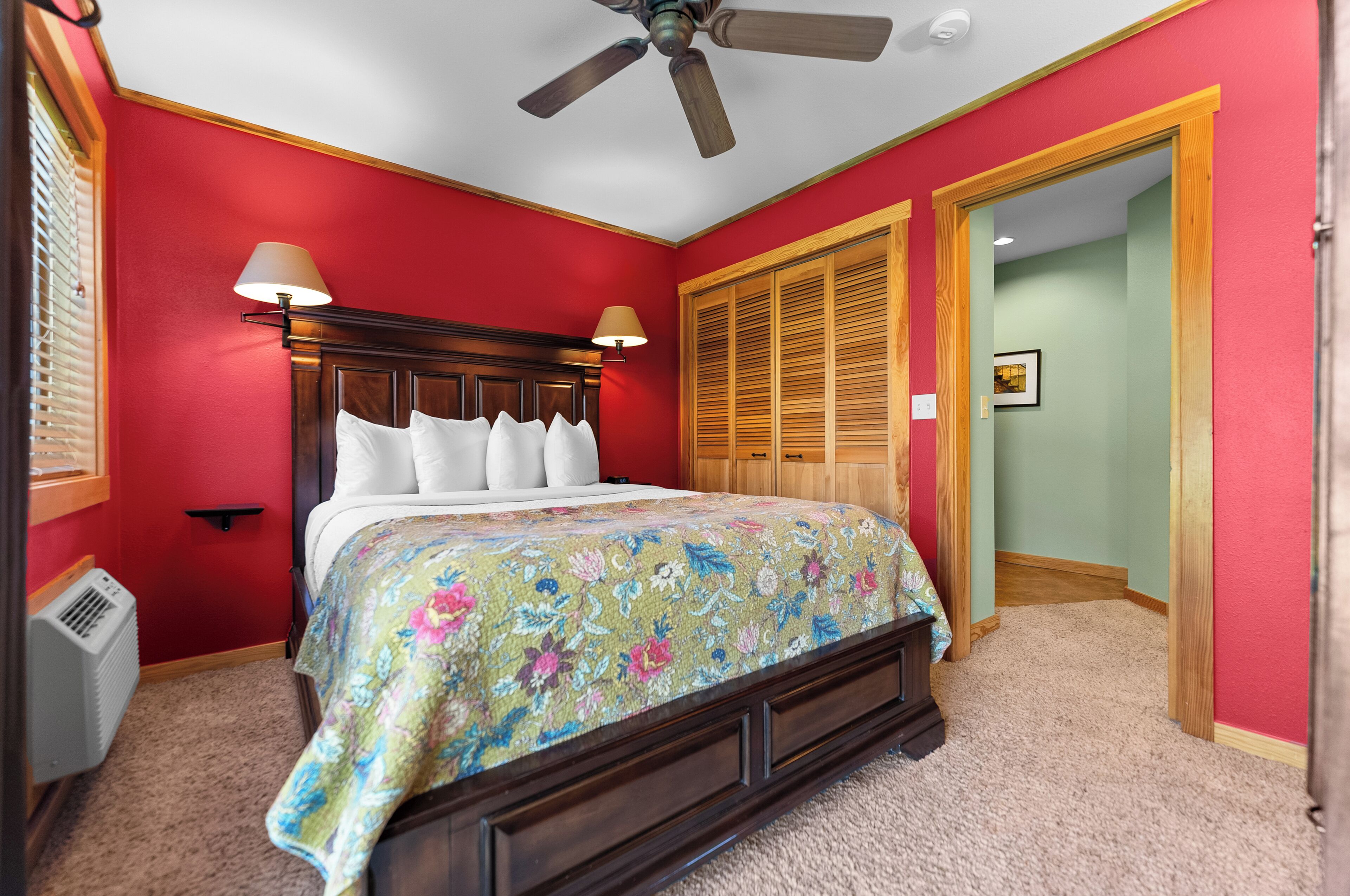 Quarto com cama de madeira, paredes vermelhas, ventoinha no teto e armário de madeira.