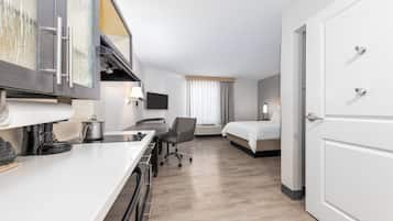 Quarto de hotel com cozinha compacta, uma cama, escrivaninha e televisão.