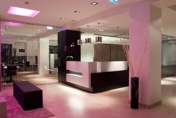 Uma área de recepção moderna com balcão, um espaço de estar com um banco e um vaso grande com galhos decorativos.