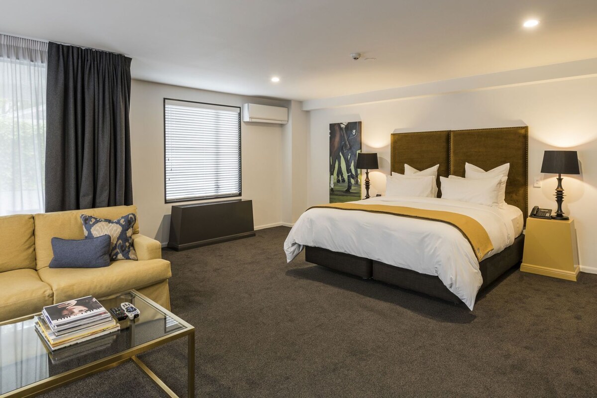 Quarto de hotel com cama, sofá, mesa de centro e um quadro na parede.