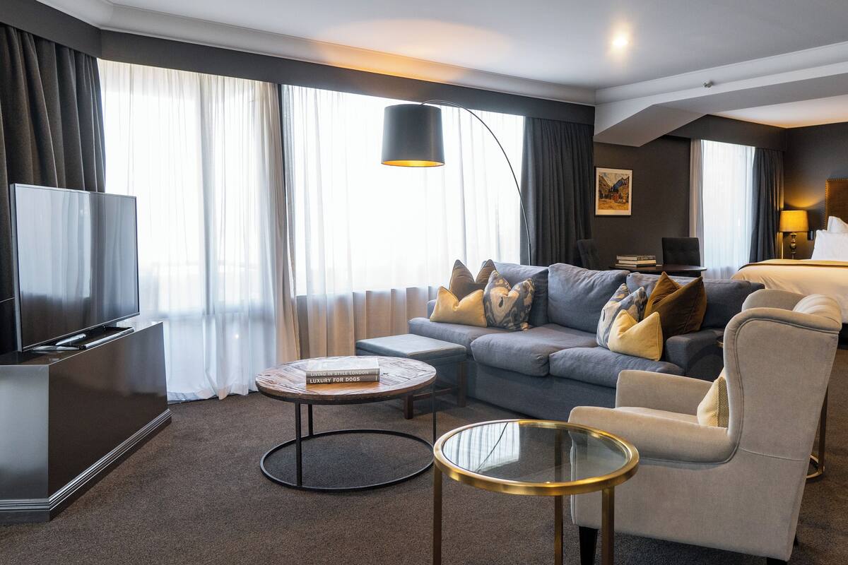 Quarto de hotel moderno com sofá, poltrona, mesa de centro redonda e uma cama.
