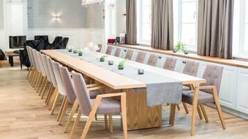 Uma longa mesa de jantar com cadeiras, um candelabro e amplas janelas com cortinas.