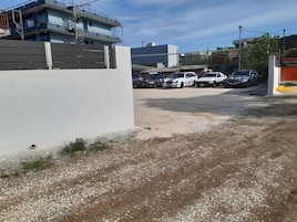 Uma área de estacionamento com vários carros, um edifício branco com varanda e uma placa indicando Hotel Oscar.